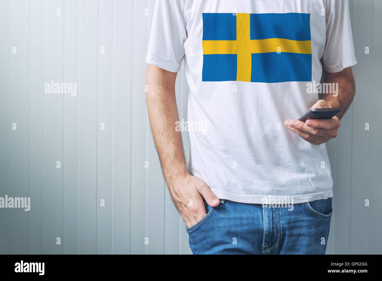 Handsome casual man with Swedish flag printed on shirt using mobile ...