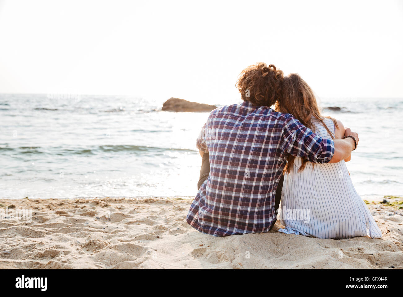 Back view of beautiful young couple sitting and relaxing on the beach ...