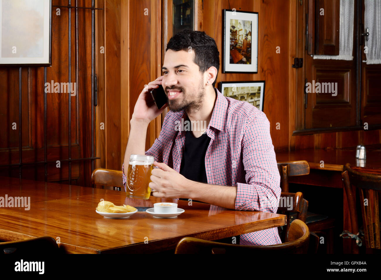 Portrait of young latin man talking on the phone with glass of beer and ...