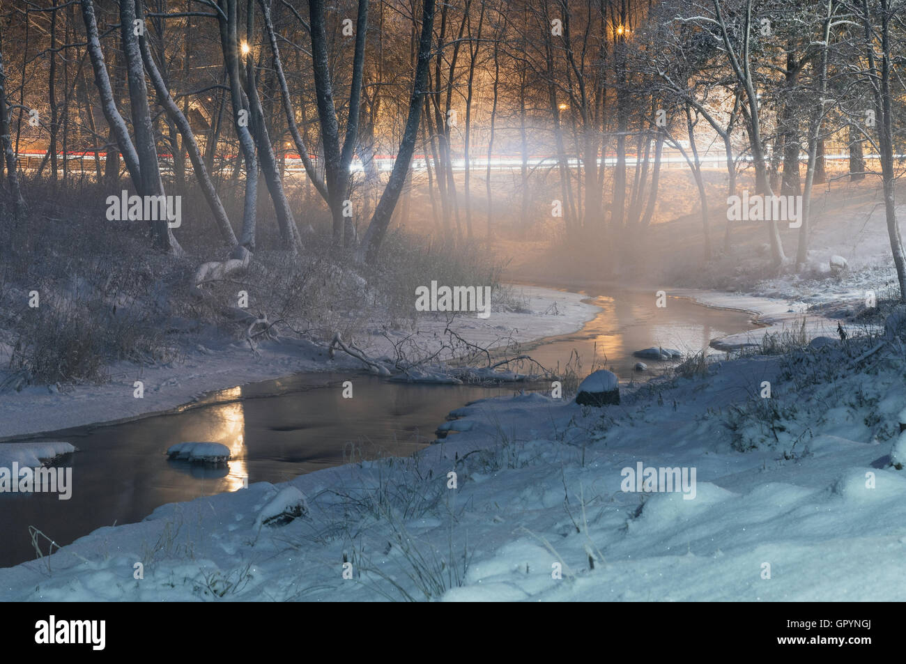 Winter-time fog over small brook in park by night. Roadway with head ...
