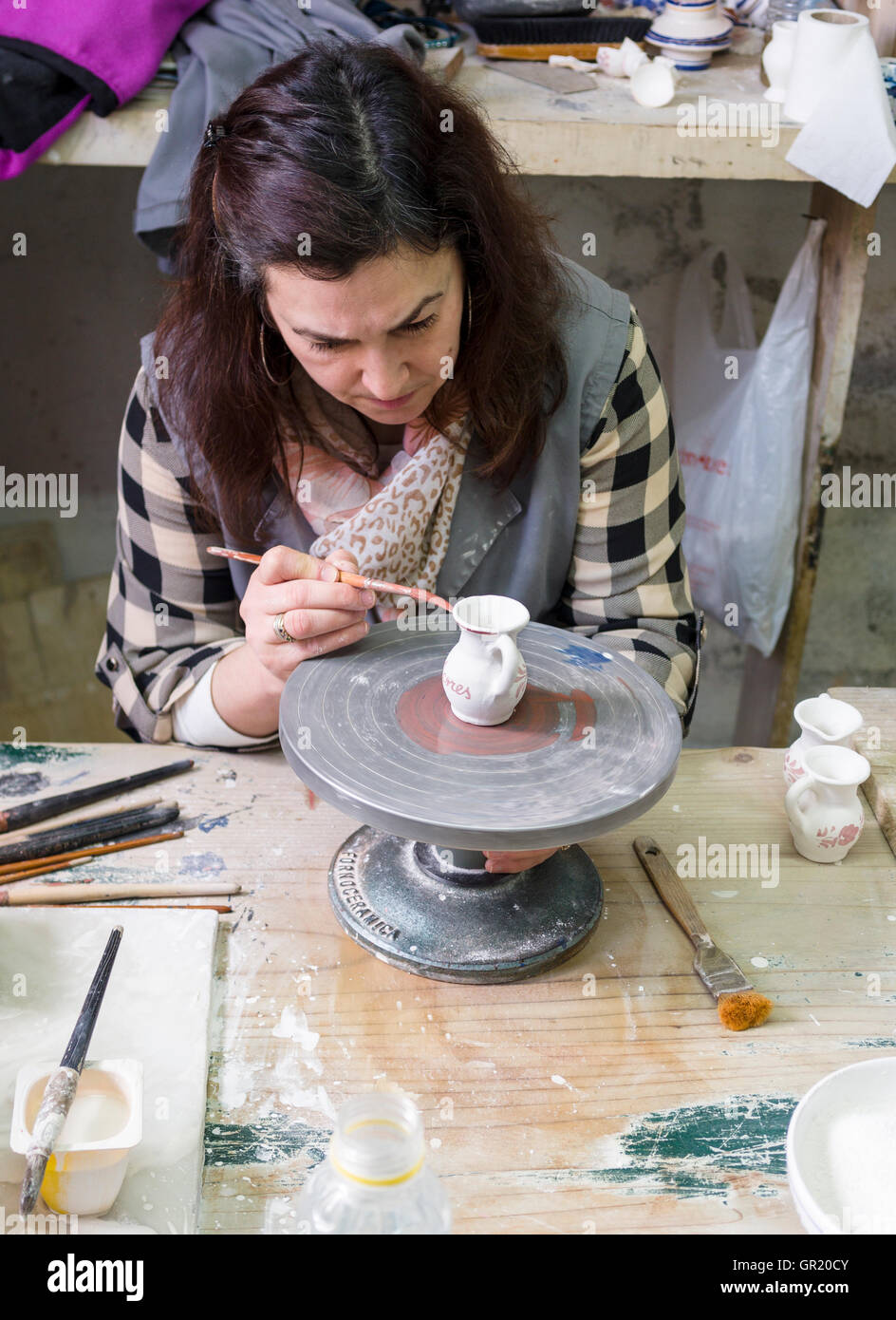 Hand painting the rim decoration on a ceramic jug. A woman worker ...