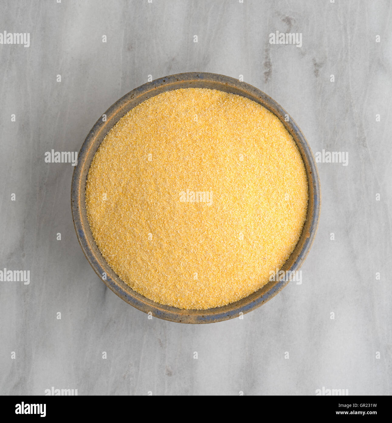 Top view of corn meal in an old bowl atop a gray marble cutting board ...