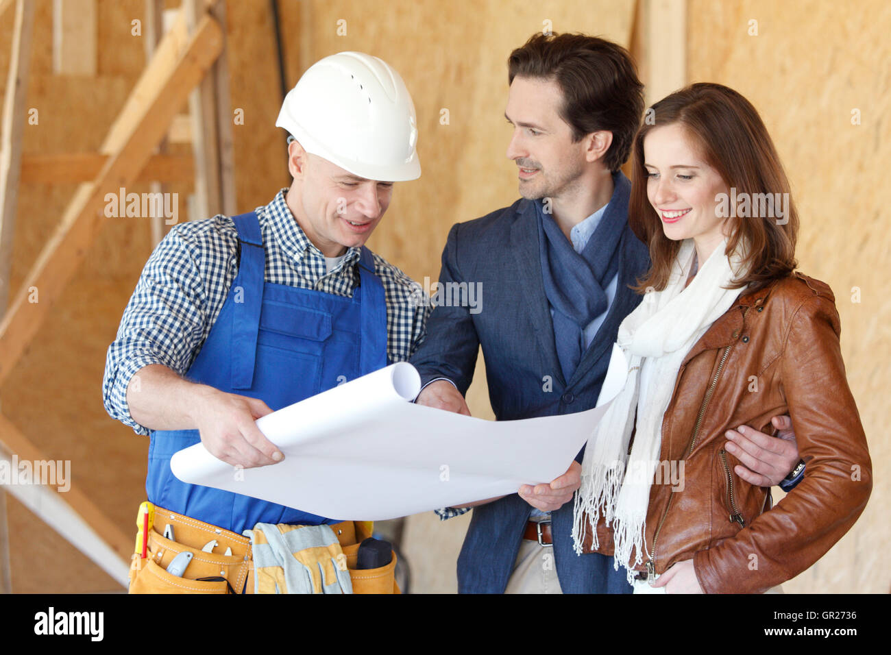 Worker shows house design plans to a young couple at construction site ...