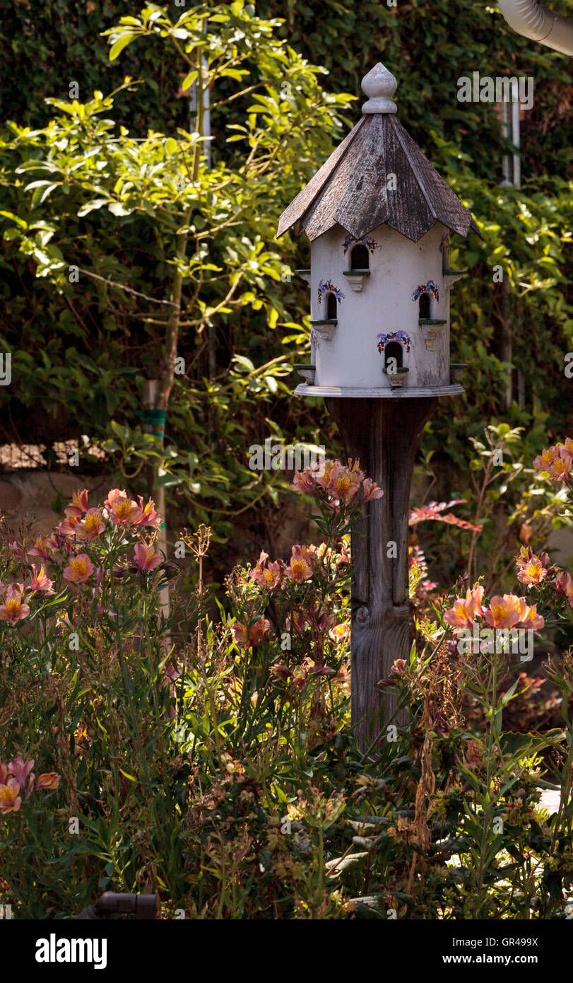 Fancy white birdhouse with custom painting on a pole in a botanical ...
