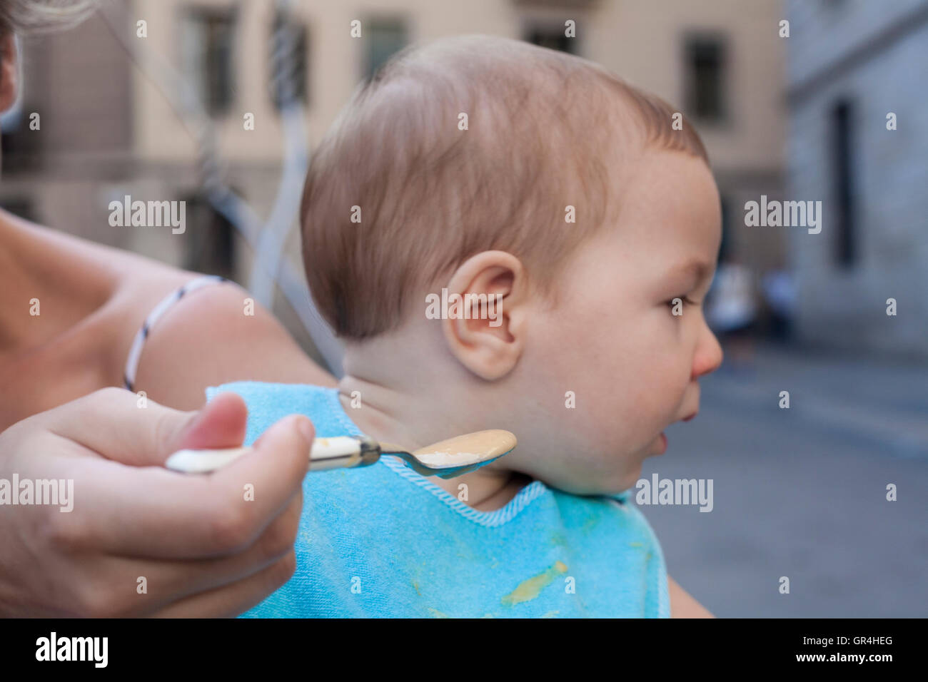 Mother trying to feed her baby boy with fruit mush although he is ...