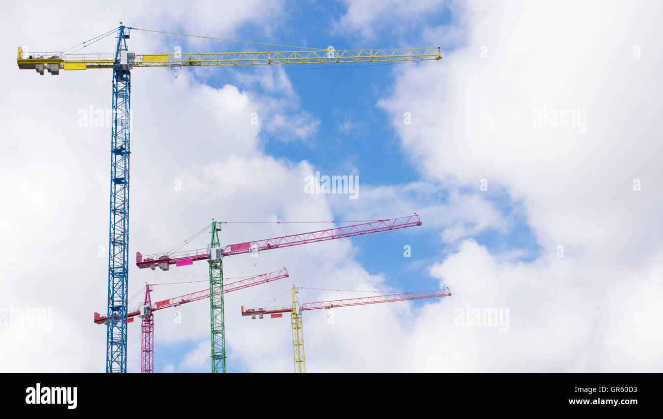 Four construction cranes painted in different bright colors with cloudy ...