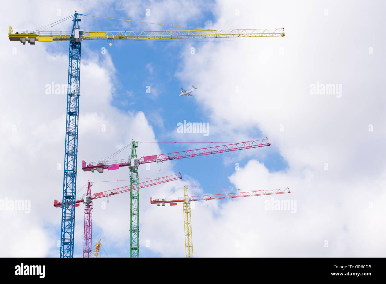 Four construction cranes painted in different bright colors with cloudy ...