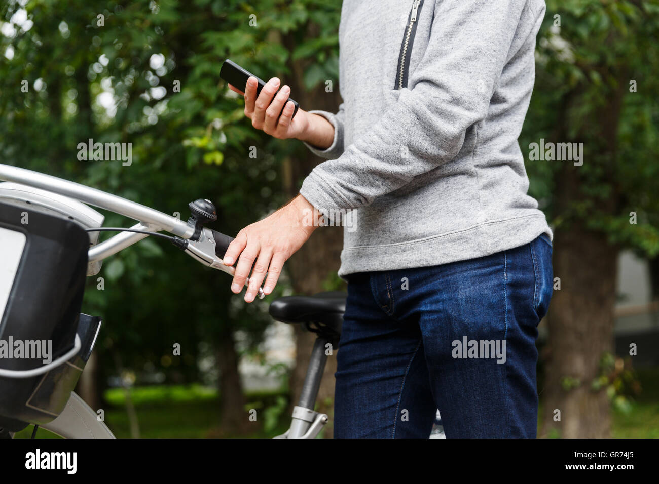 Guy standing next to his bike and holding cell phone Stock Photo - Alamy
