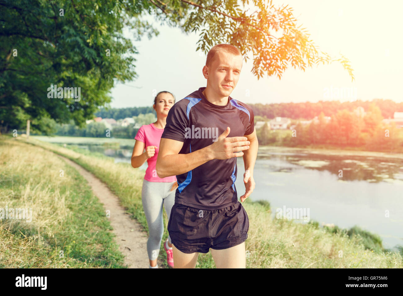 Young athletic people jogging outdoor near pond. Man and woman doing ...