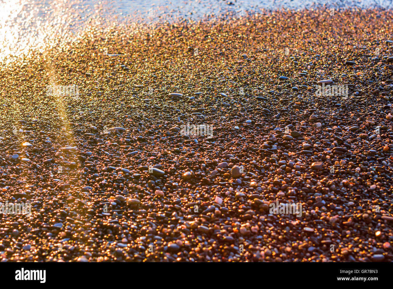 Sea pebbles, shore of beach is covered in glittering sun stones. Stone ...