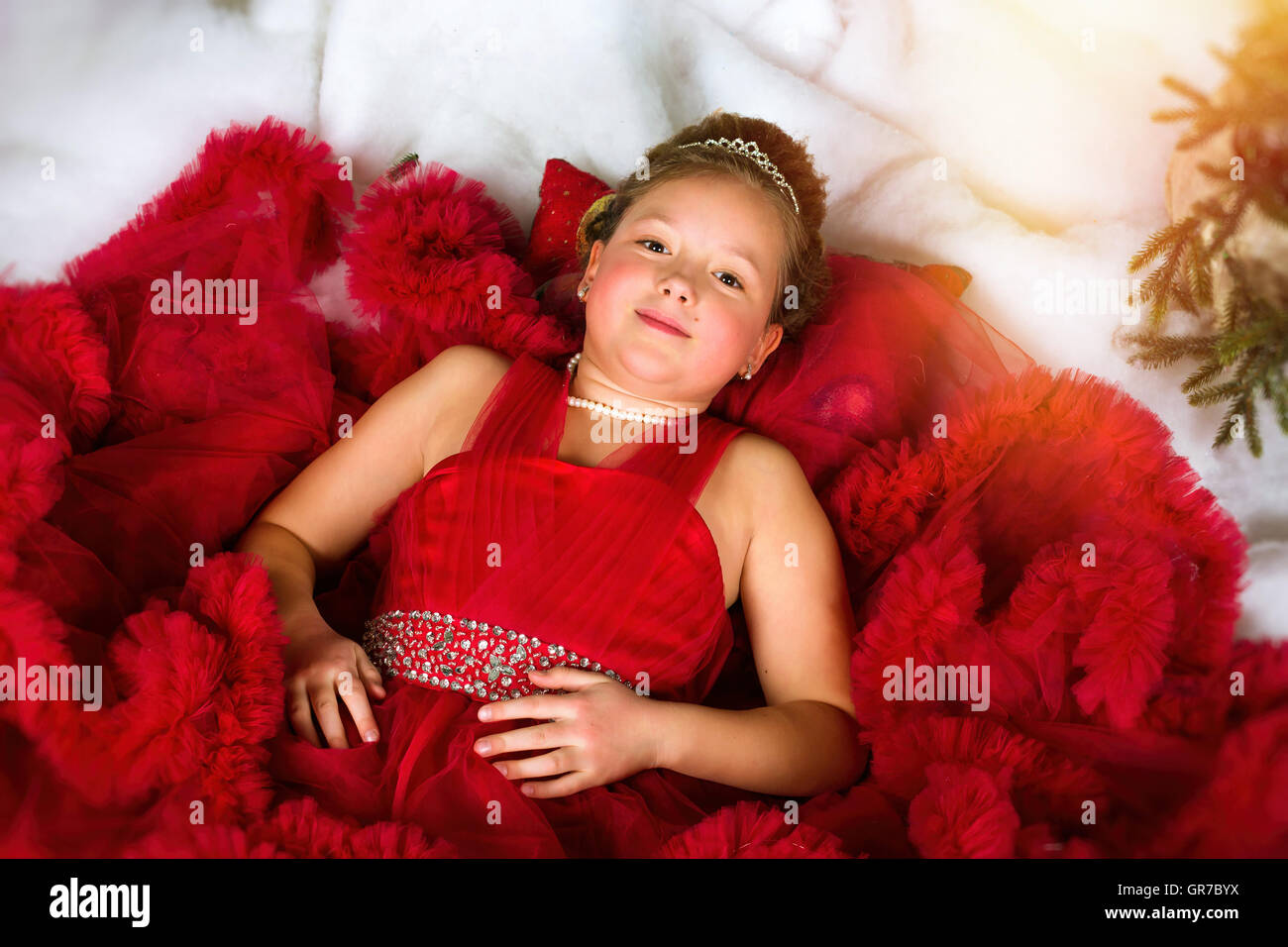 Little winter Princess in a precious crown in red dress lies on ...