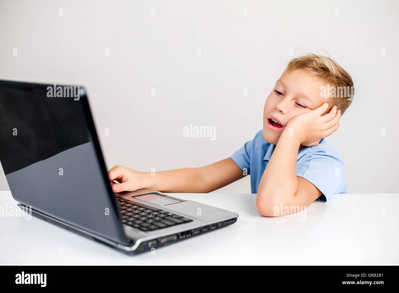 bored kid using laptop at table Stock Photo - Alamy