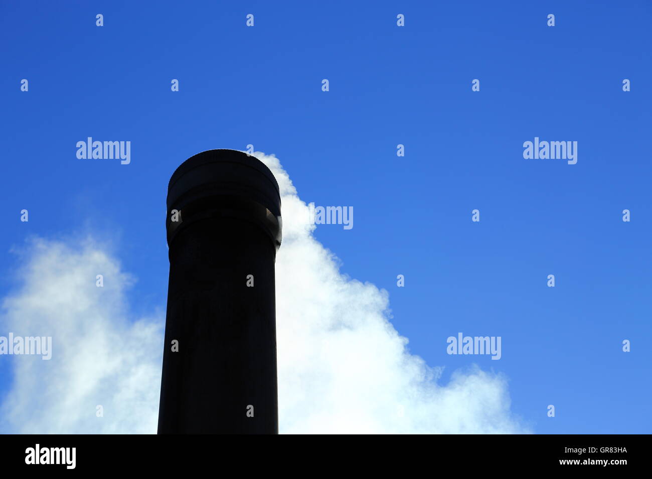 Smoke pours out of a chimney under a vibrant clear blue sky. CO2 ...