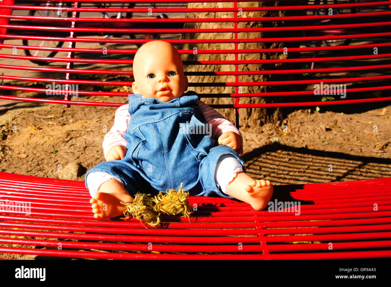 Doll Without Hair On A Red Metal Bench Stock Photo - Alamy