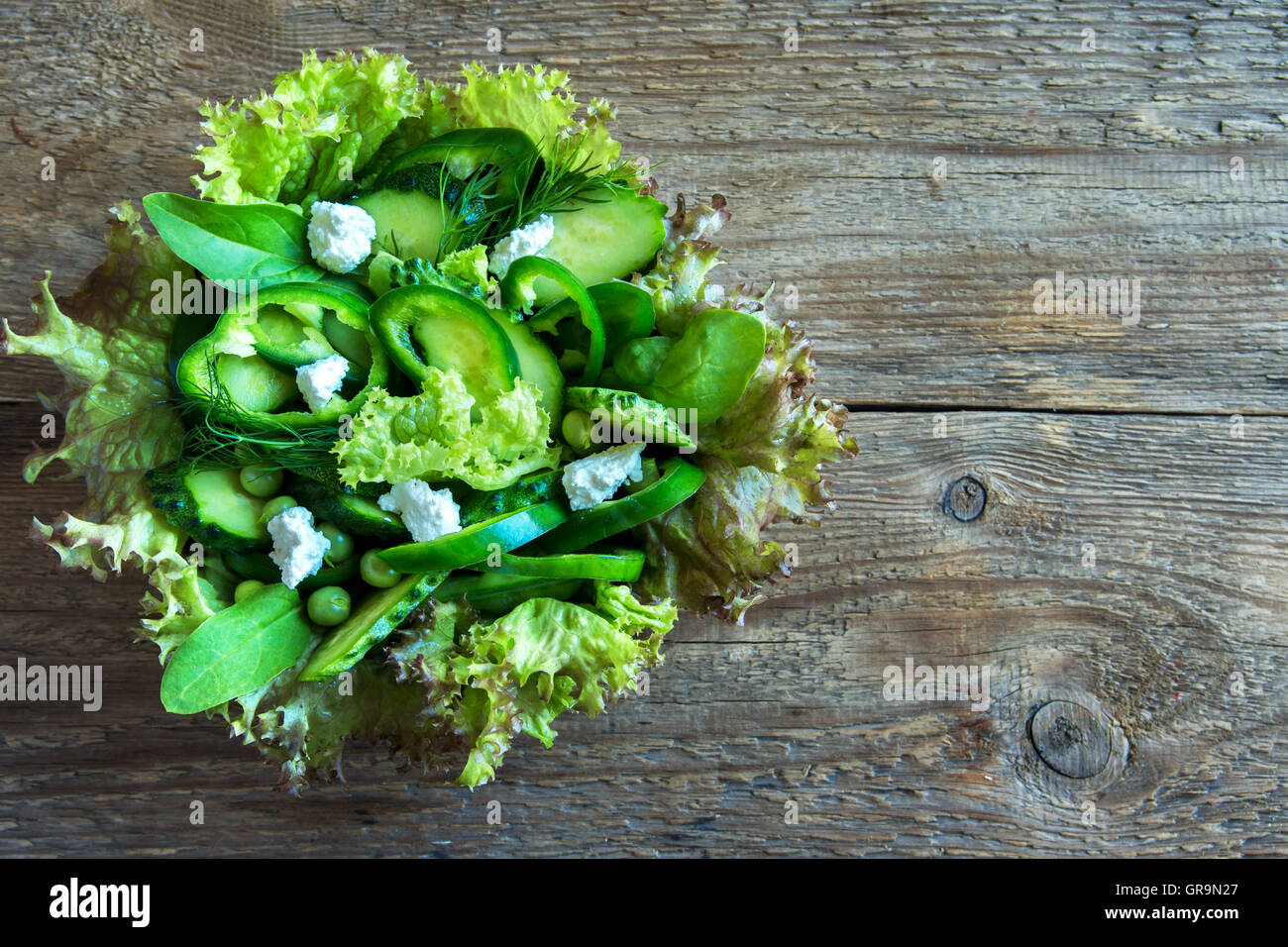 Organic mixed green vegetable salad with feta cheese over rustic wooden ...