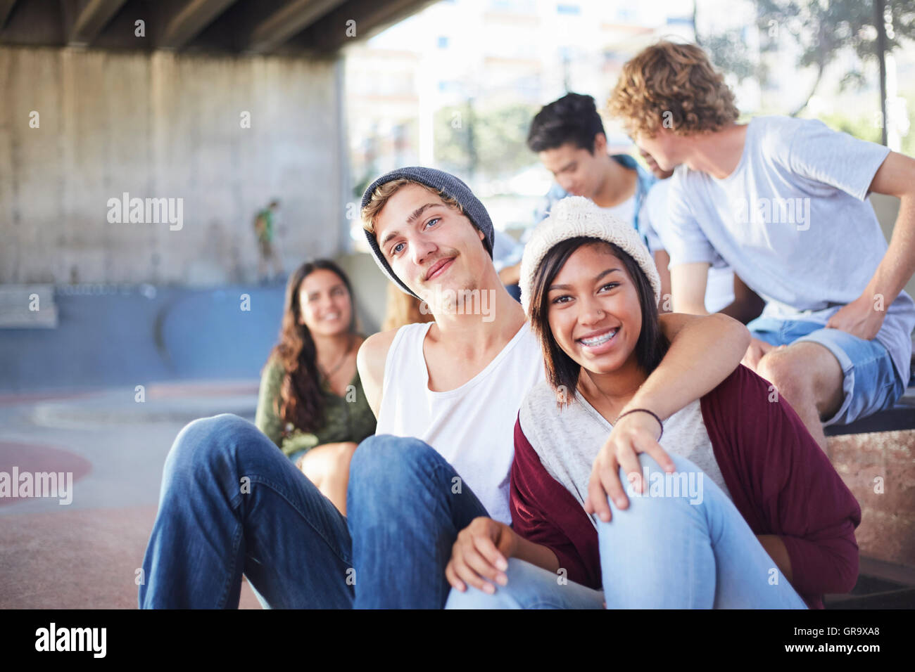 Portrait smiling teenage couple hanging out with friends at skate park ...