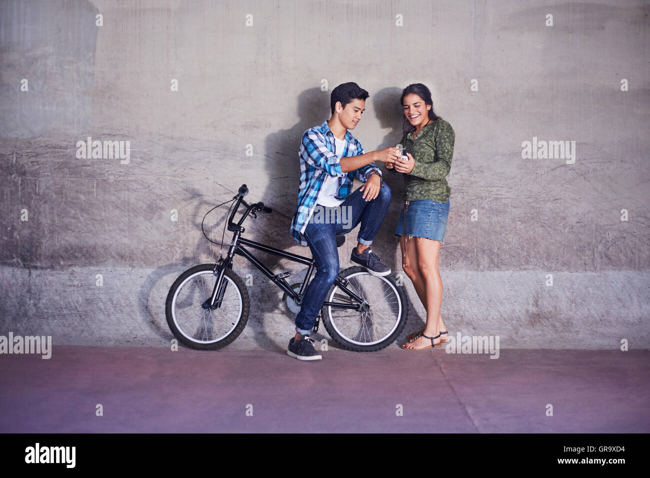 Teenage couple with BMX bicycle texting at wall Stock Photo - Alamy