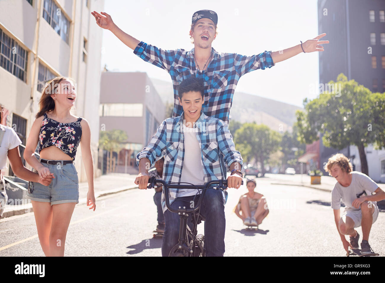 Teenage friends riding BMX bicycle and skateboarding on sunny urban ...