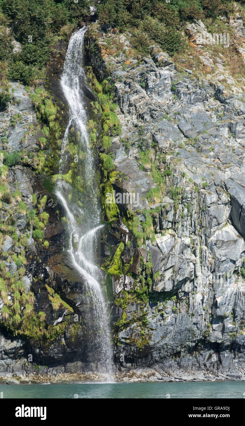 A narrow waterfalls cascades down a rocky face into the bay Stock Photo ...