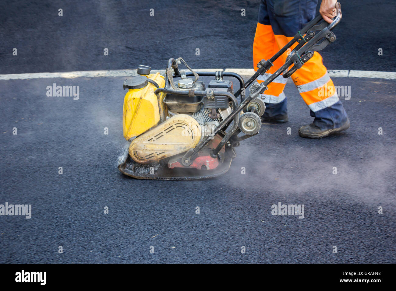 Worker use vibratory plate compactor compacting asphalt at road repair ...
