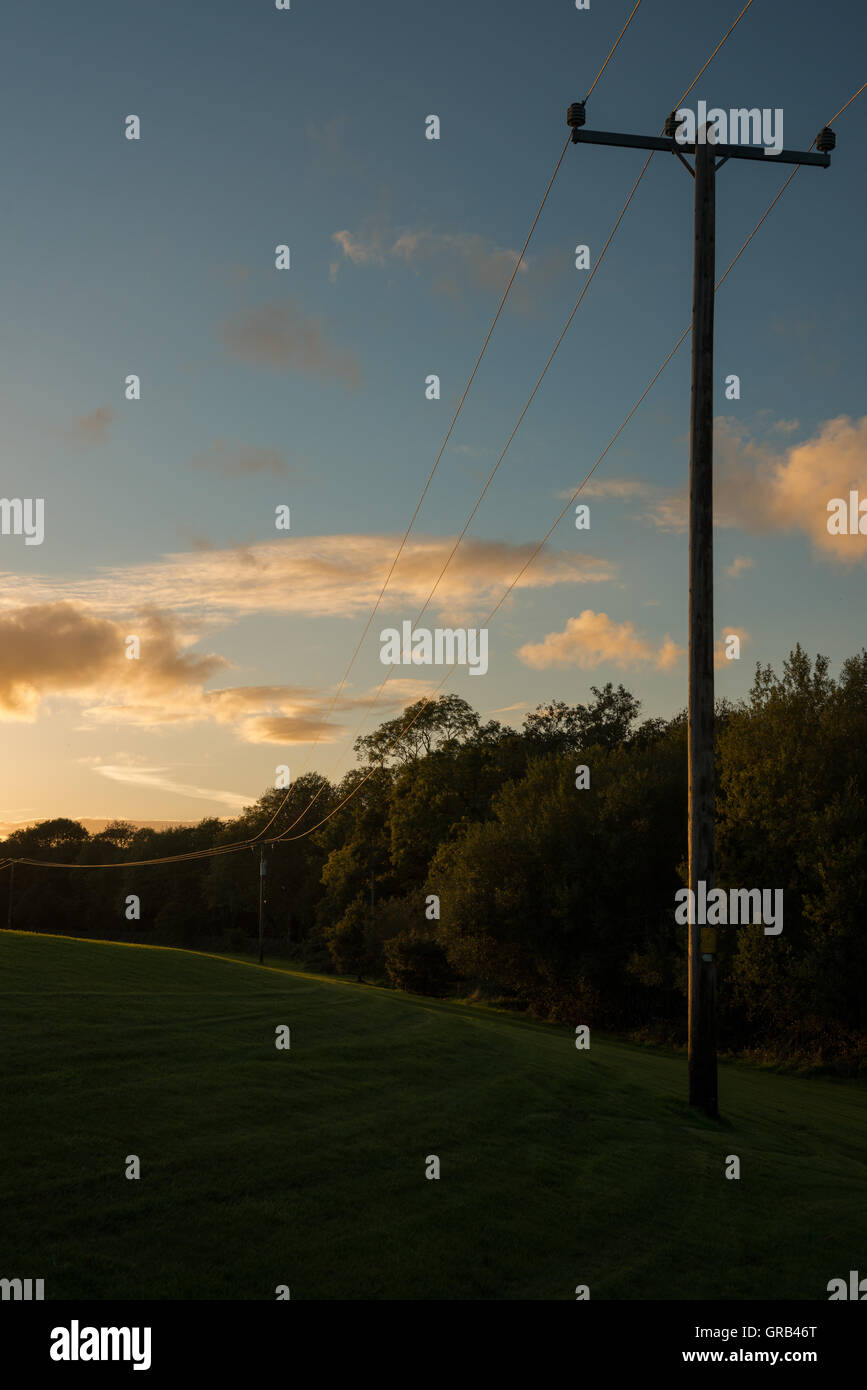Wooden power line pole and overhead electrical power lines at sunset ...