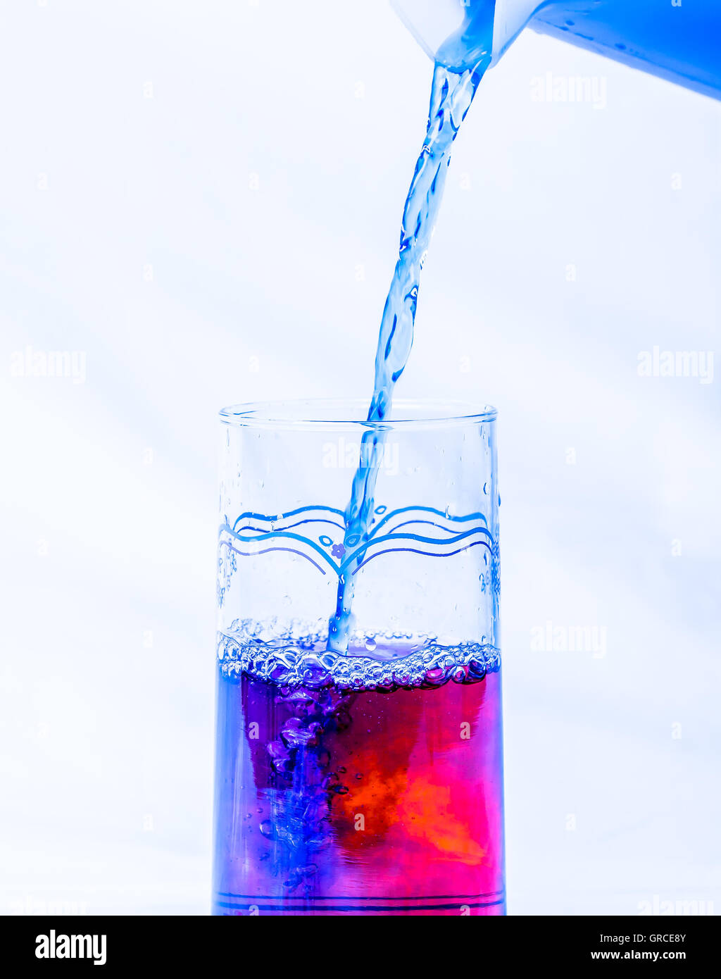 A pitcher of blue liquid being mixed in a glass of red liquid Stock ...
