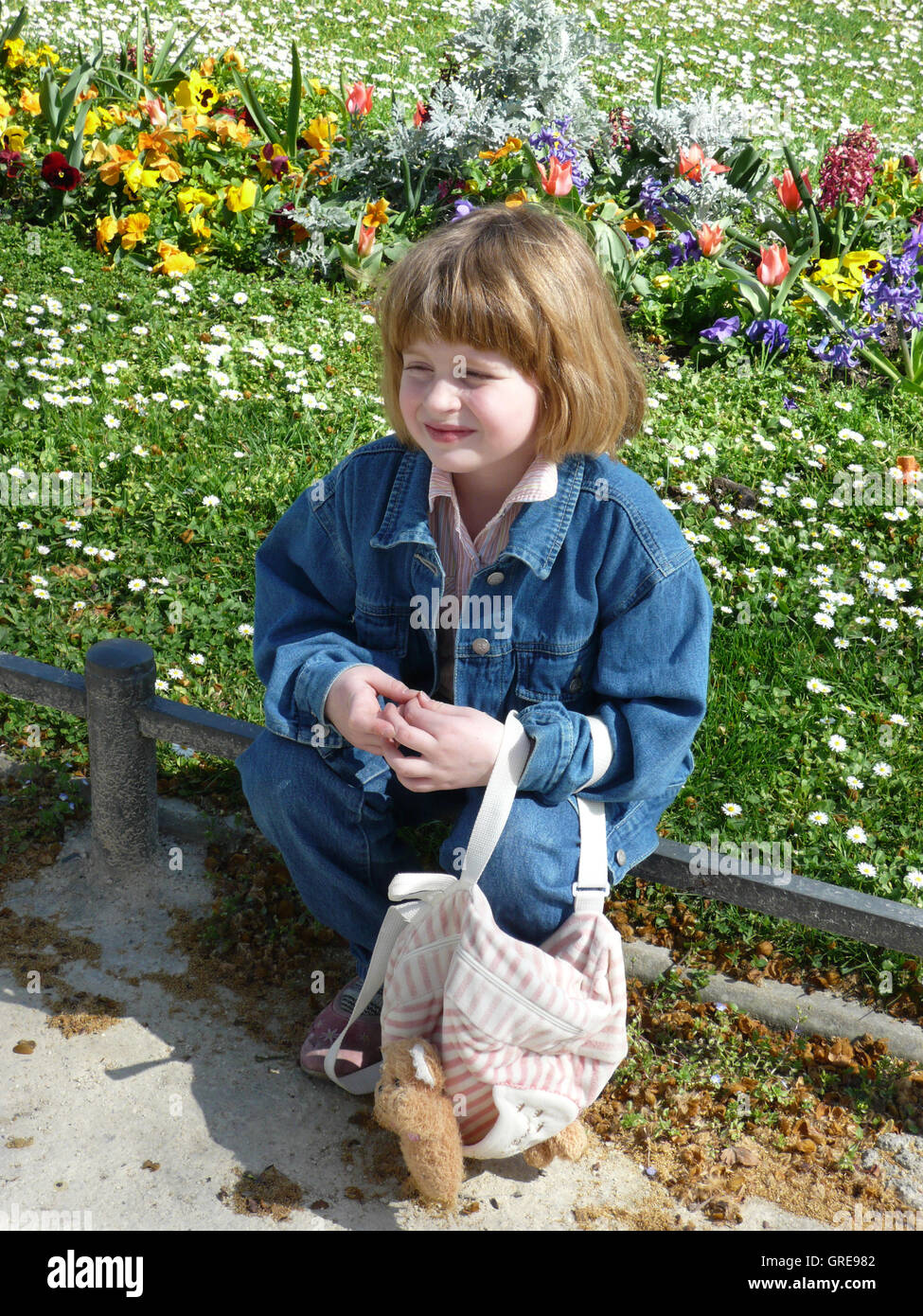 Little Girl In The Park Sitting In Front Of Flower Beds Stock Photo - Alamy