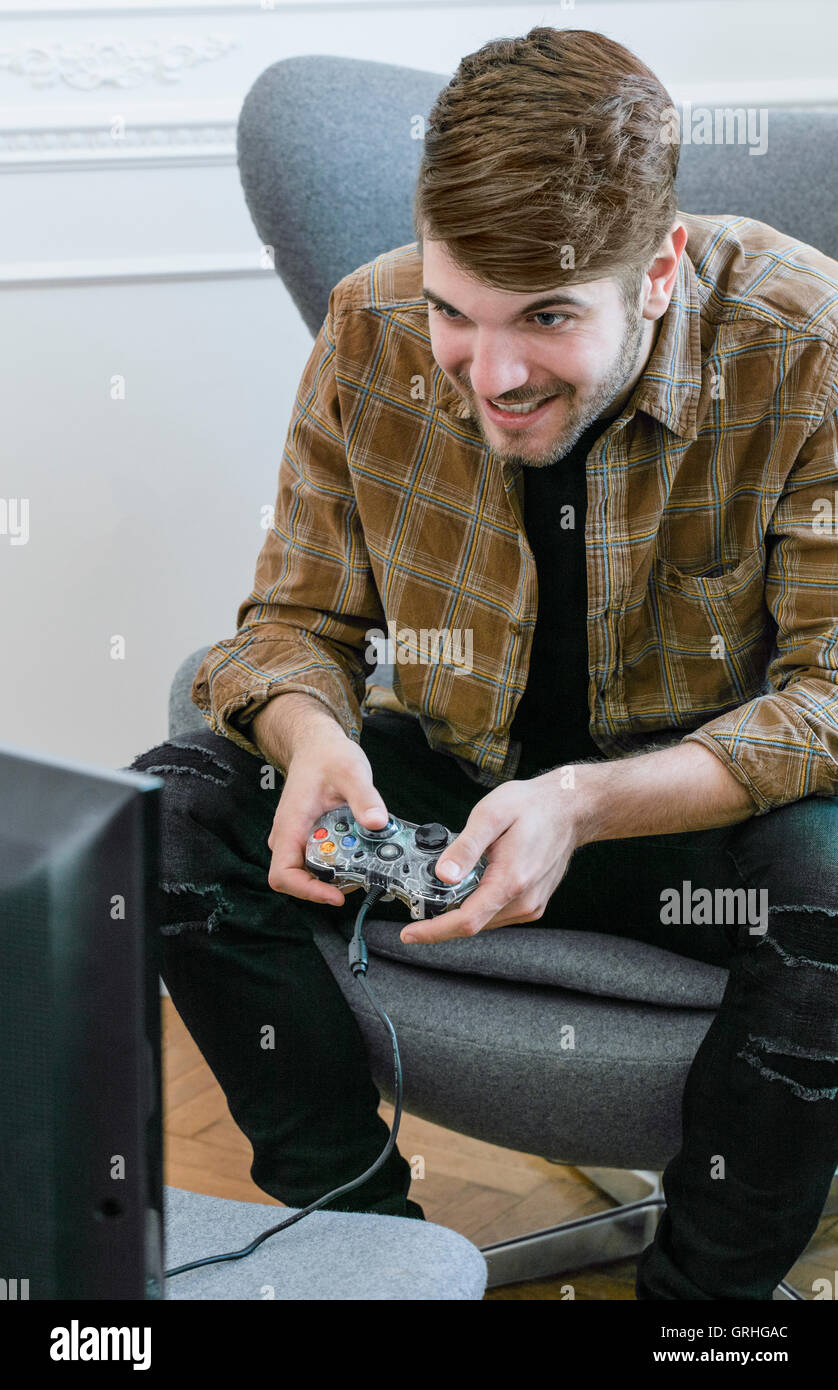 A Young dark haired man leans forward in his chair while holding a game ...