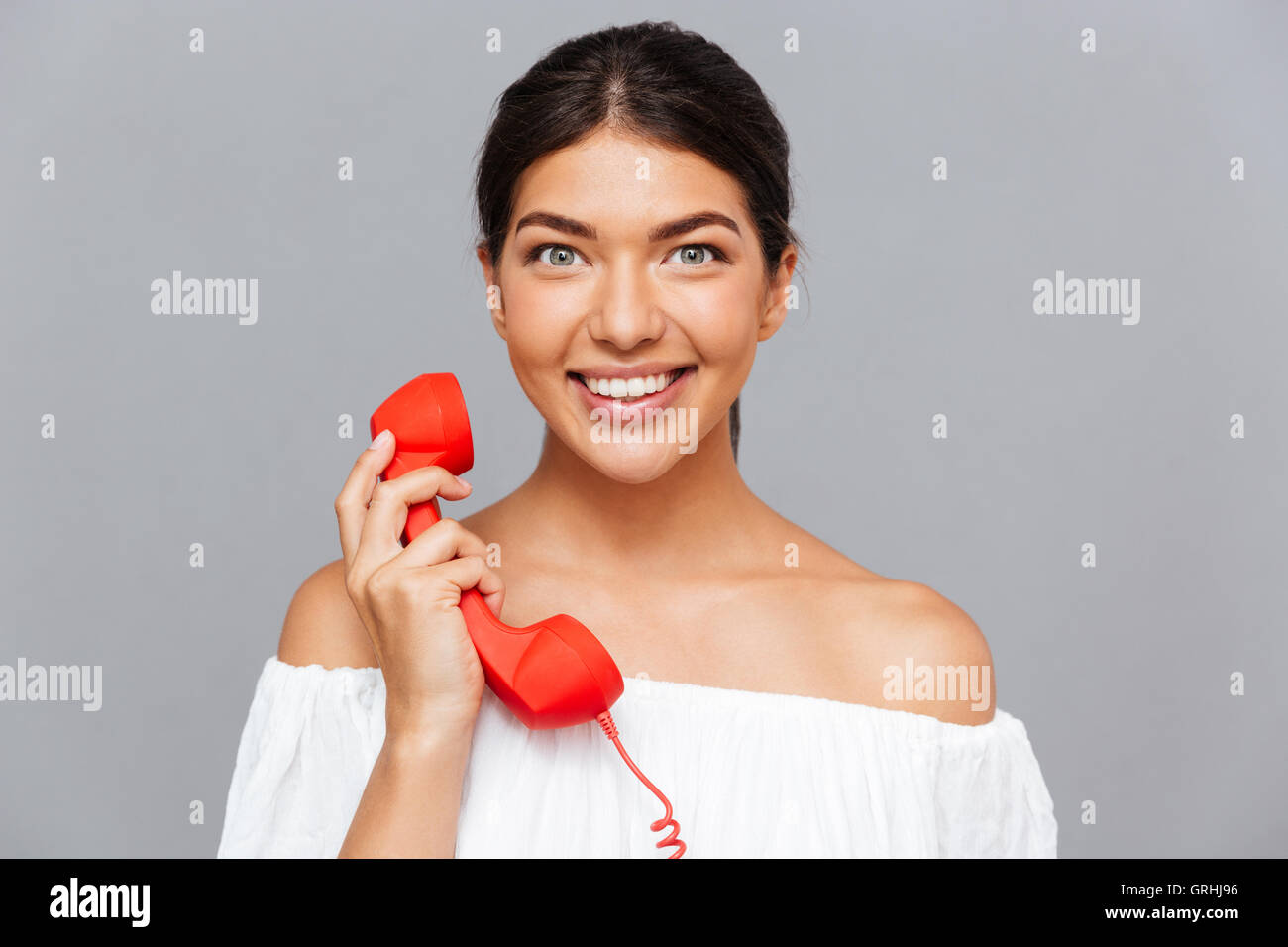 Cheerful woman talking on the phone tube and looking at camera isolated ...