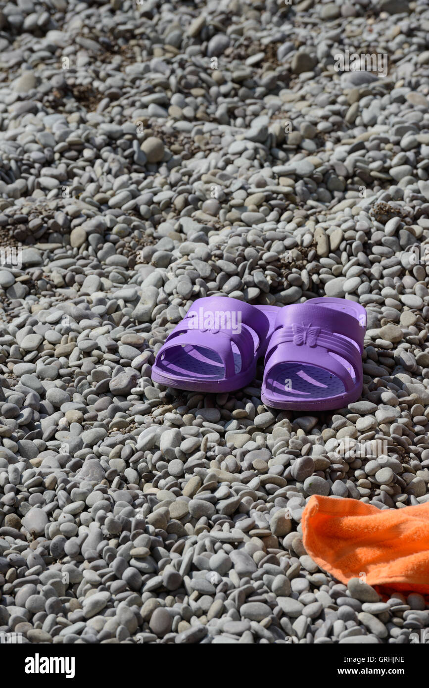 Pair of bright purple beach sandals are on the grey pebble in sunlight ...