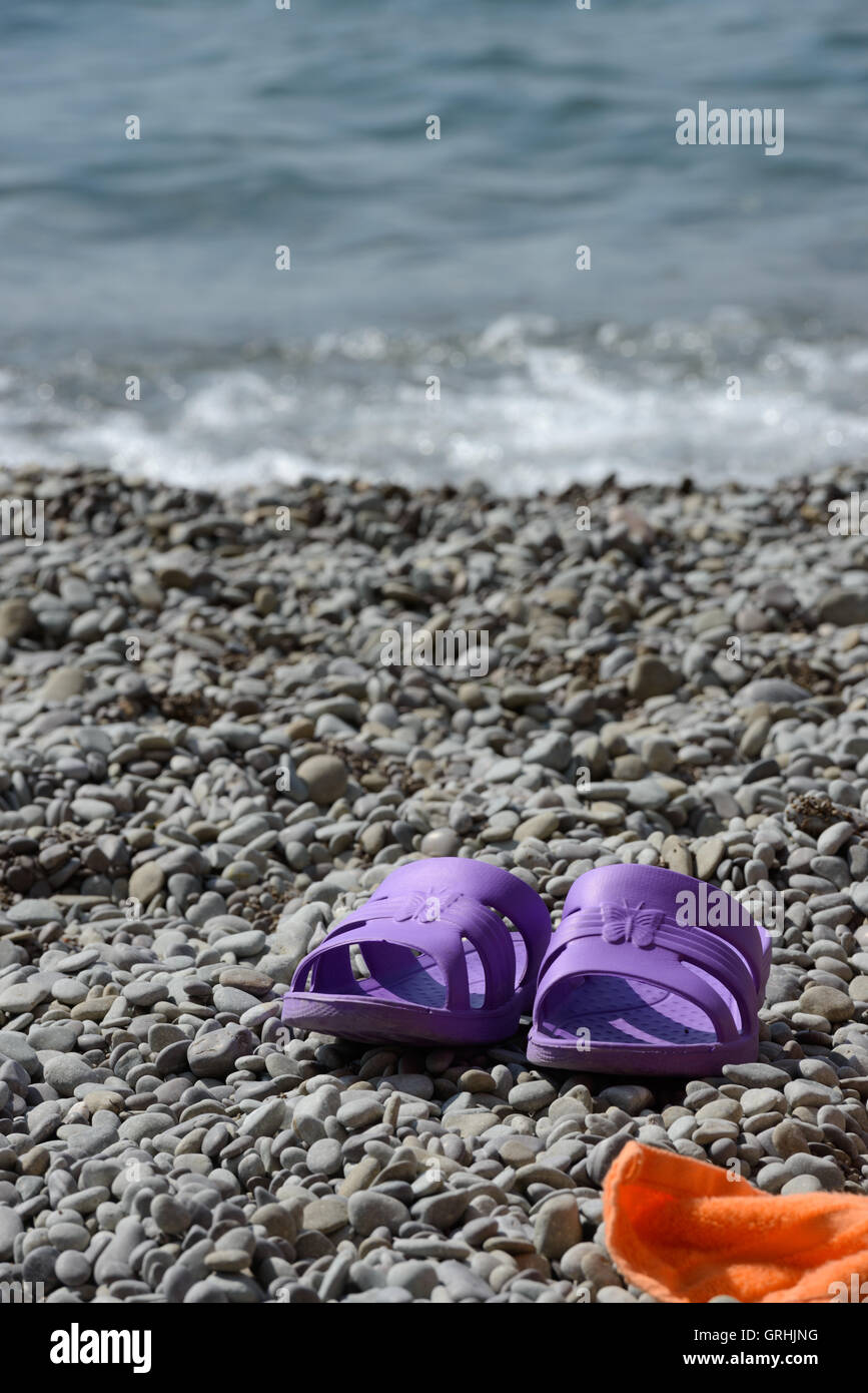 Pair of bright purple beach sandals are on the grey pebble in sunlight ...
