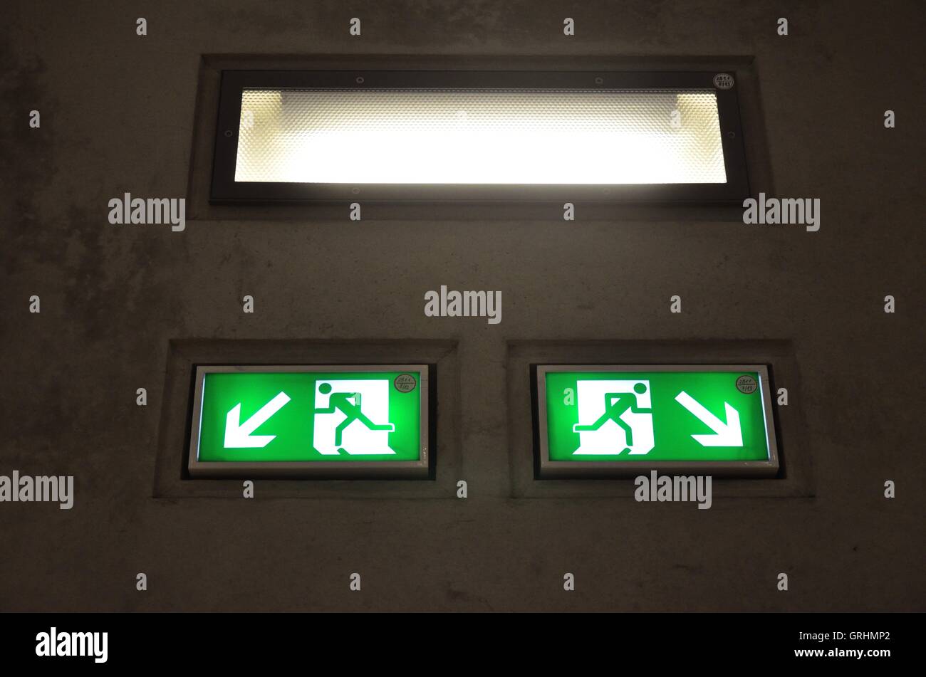 Two way green exit sign on concrete wall Stock Photo - Alamy