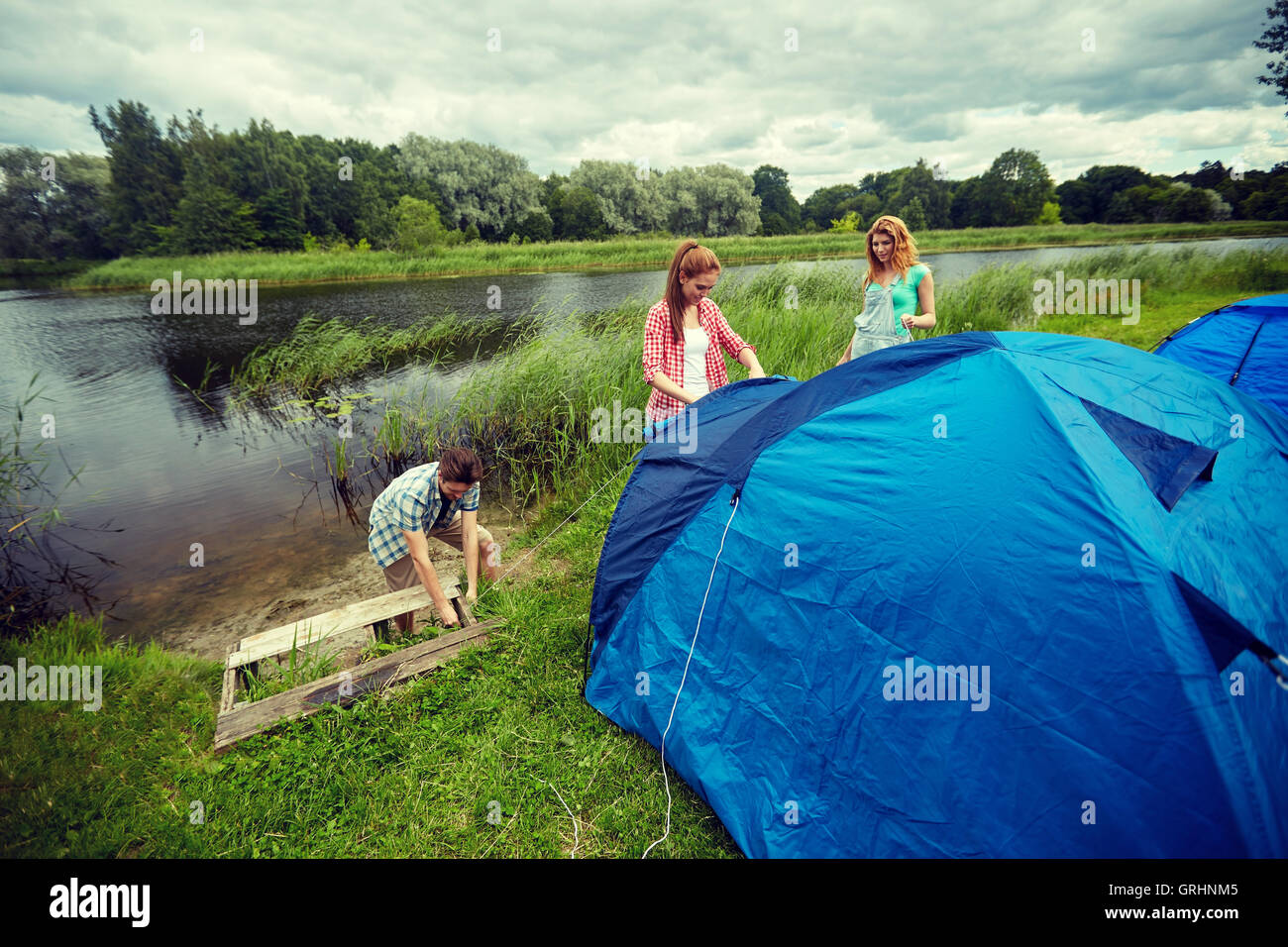 group of smiling friends setting up tent outdoors Stock Photo - Alamy