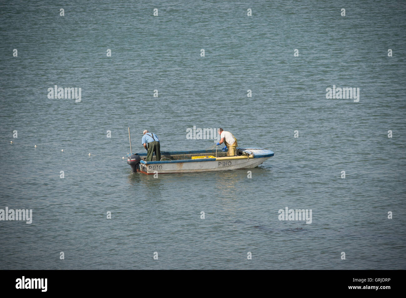 two fishermen catching fish with nets from a small boat in Portsmouth ...