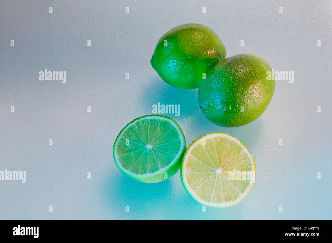 Three limes, one of them cut in two halves Stock Photo - Alamy