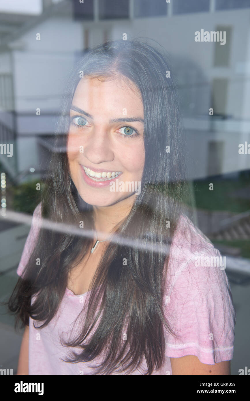 Portrait of a young beautiful woman looking outside through window ...