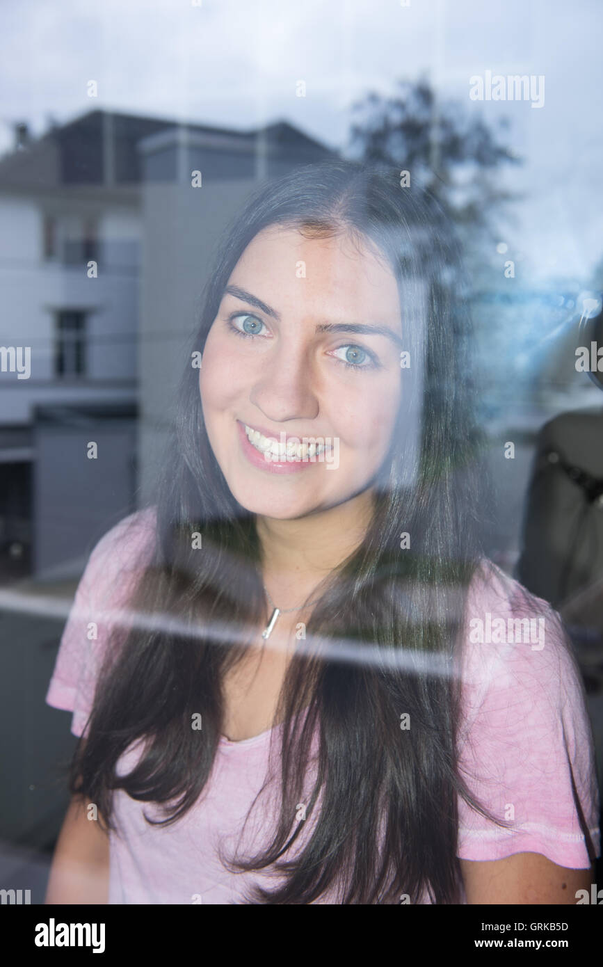 Portrait of a young beautiful woman looking outside through window ...