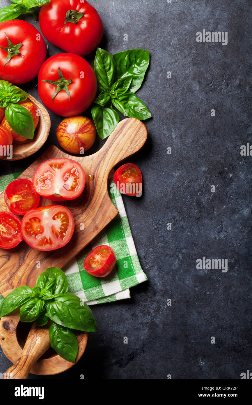 Fresh ripe garden tomatoes and basil on stone table. Top view with copy ...