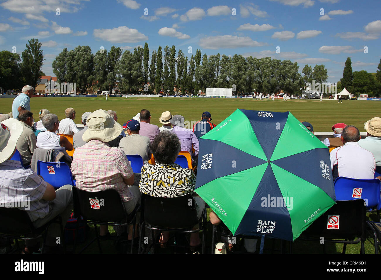 A spectator shelters under an umbrella as play progresses on a hot day ...