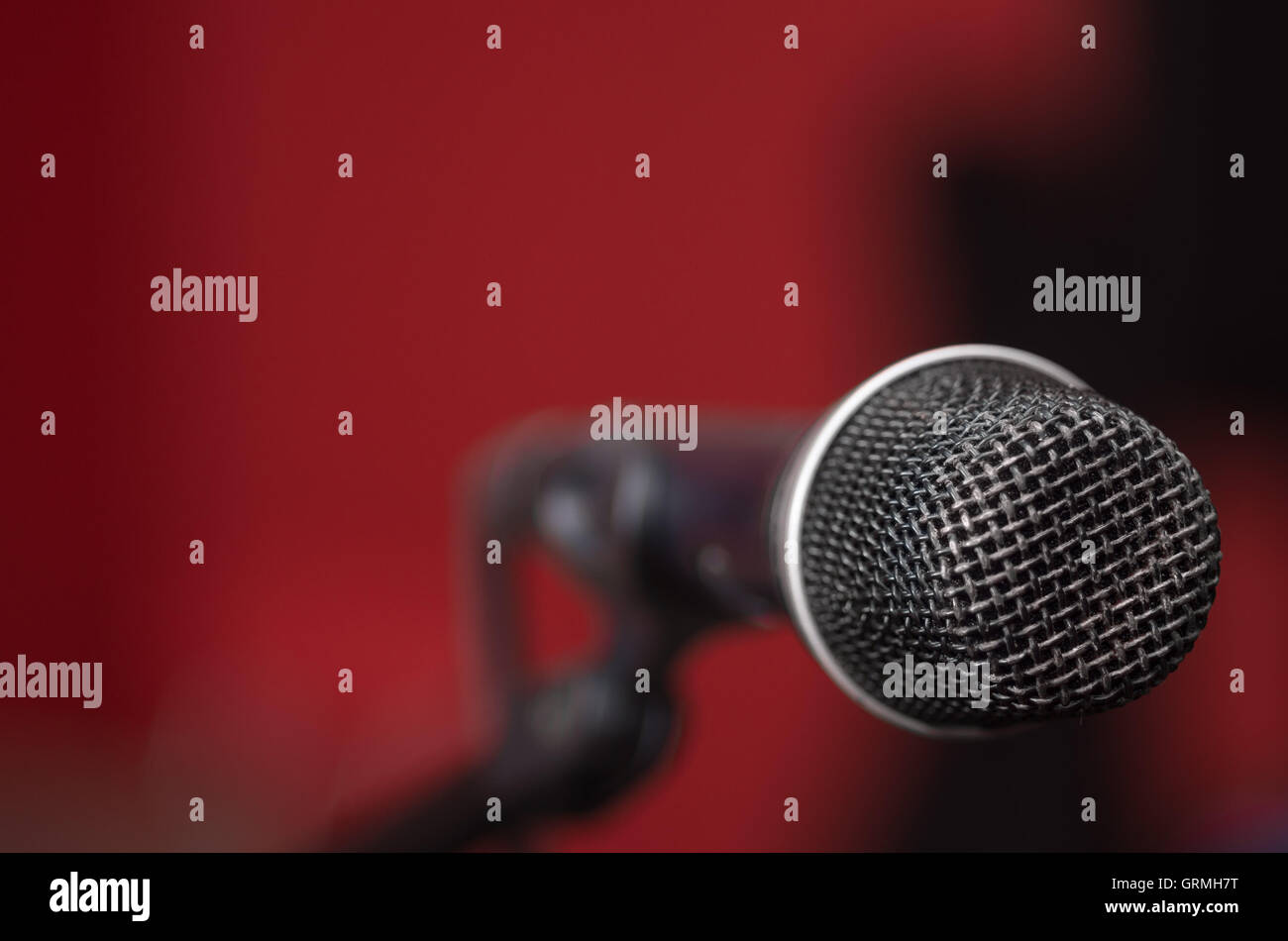 Closeup black vocal microphone mounted on mic stand, blurry red dark ...