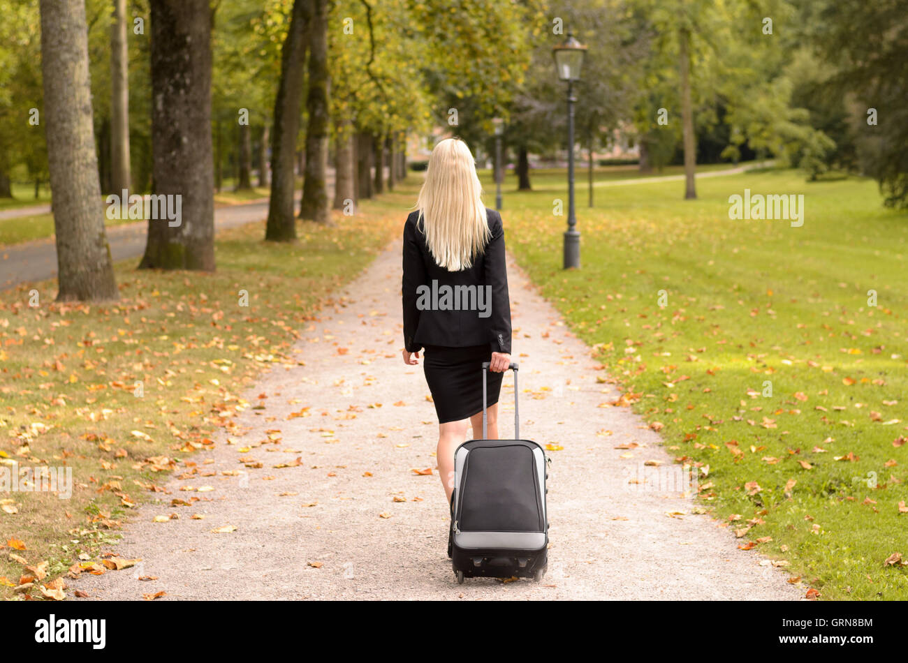Blond professional in a black suit woman pulling a suitcase behind her ...