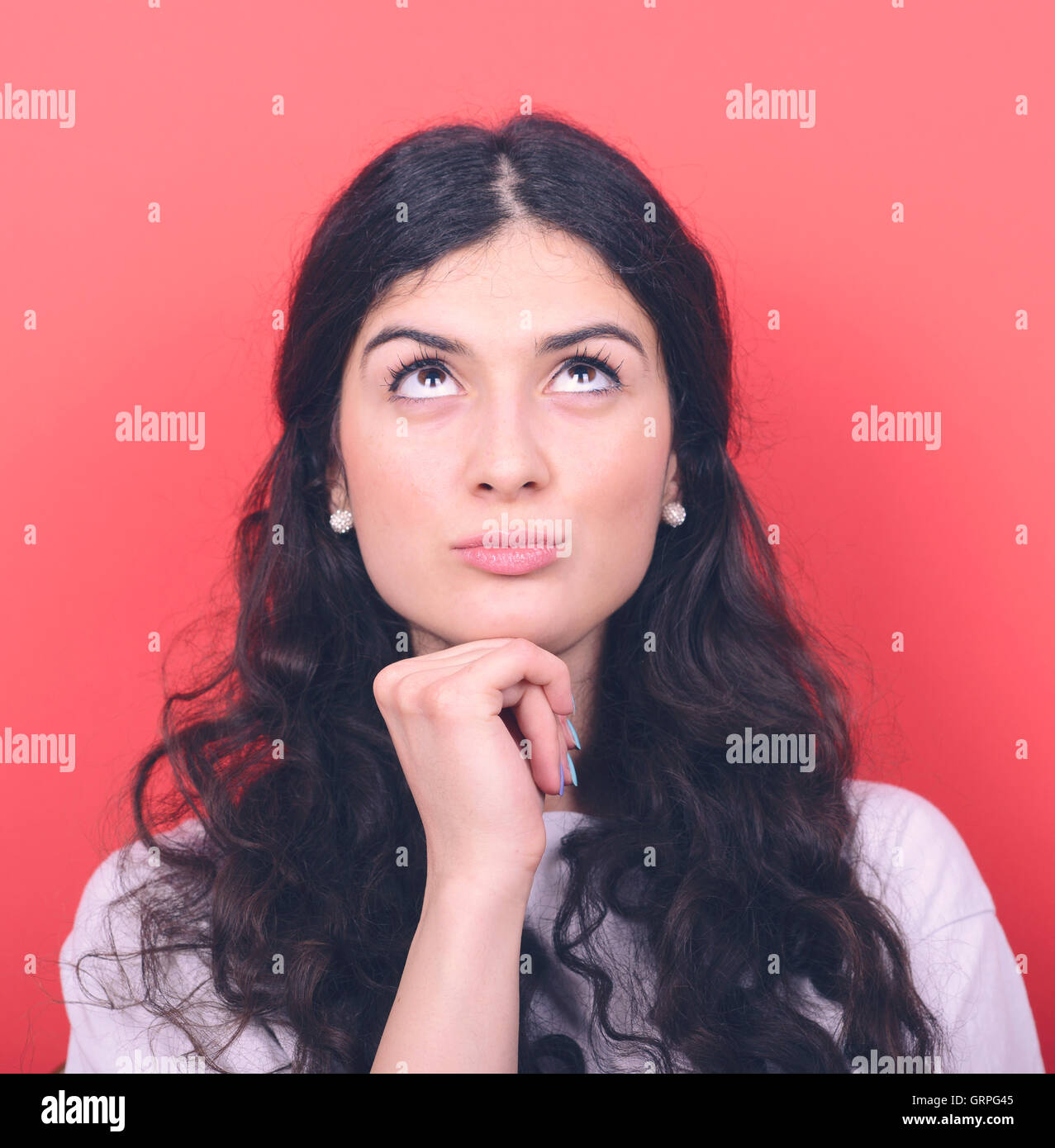 Portrait of beautiful girl thinking and looking up against red ...