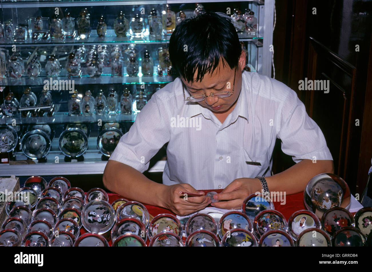 Chinese artist painting the inside of glass balls and small bottles ...