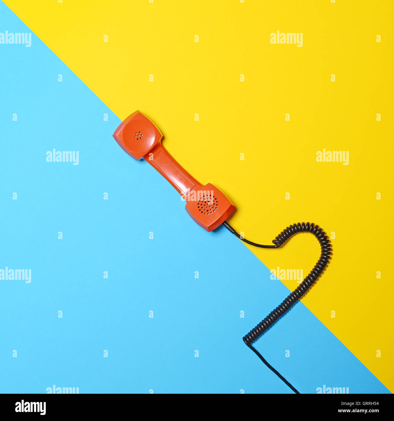 Retro orange telephone tube on striped blue and yellow background ...