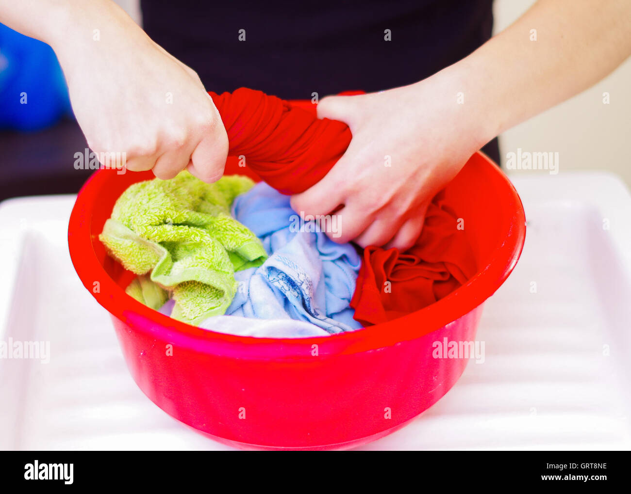 Closeup womans hands handwashing clothes in red plastic washbucket ...