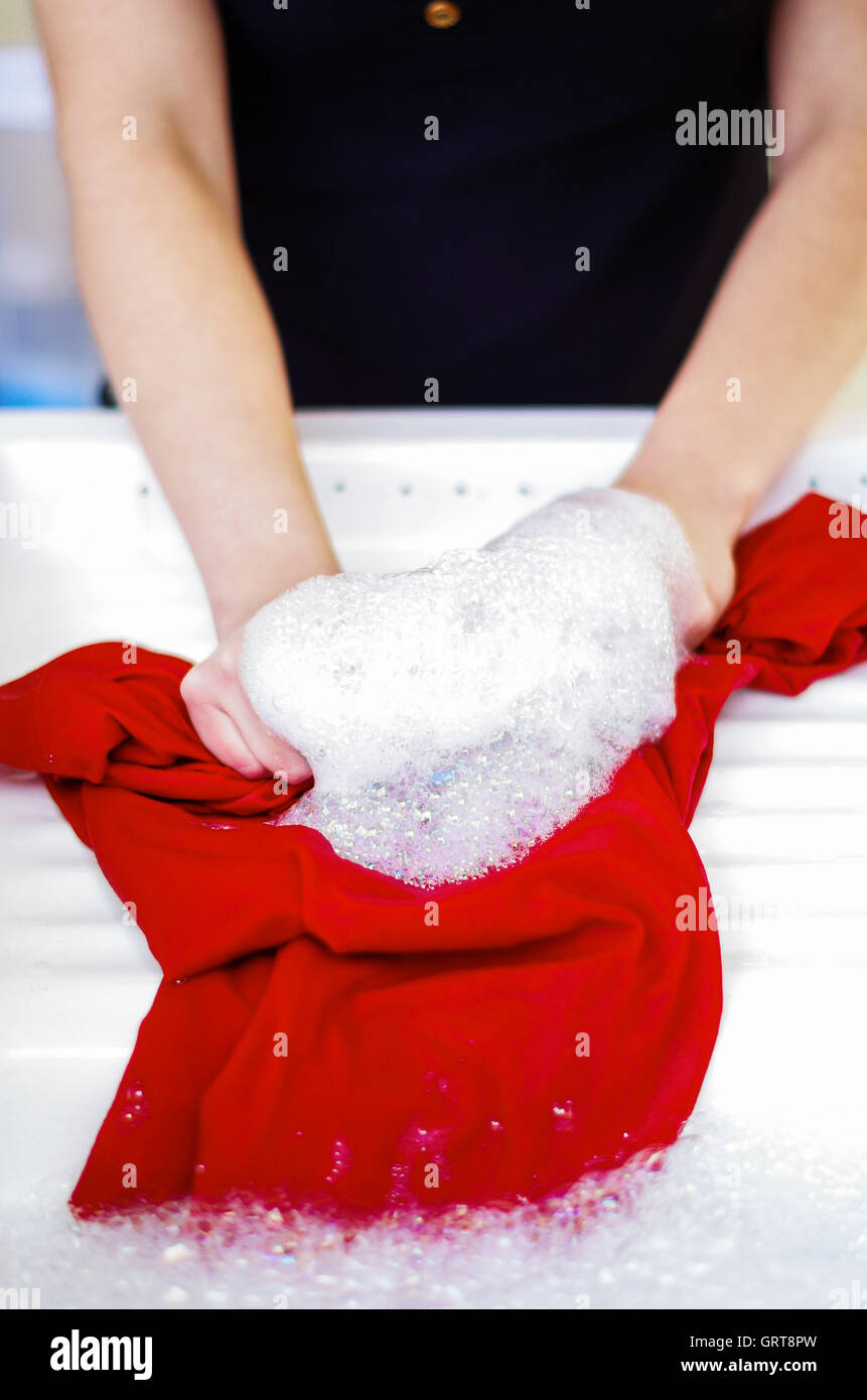 Closeup womans hands handwashing clothes in red plastic washbucket ...