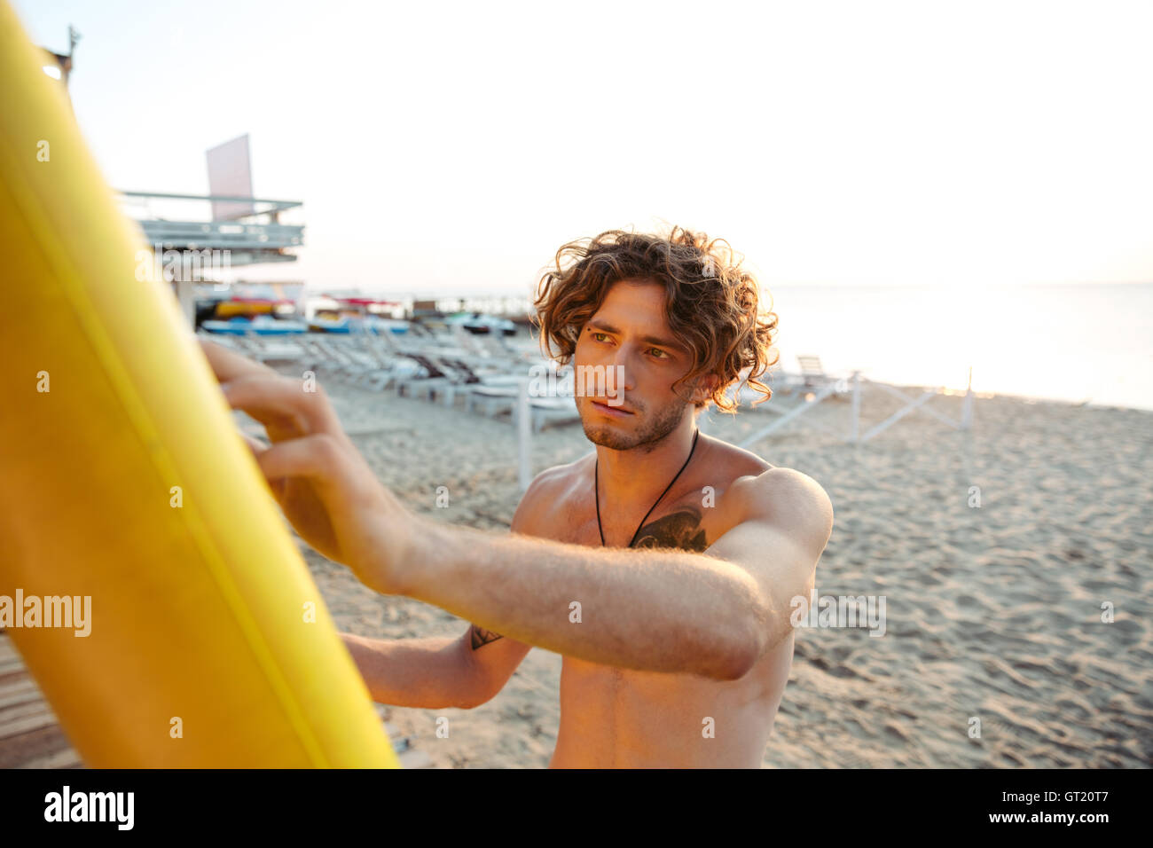 Professional young surfer getting board ready for surf at the beach ...