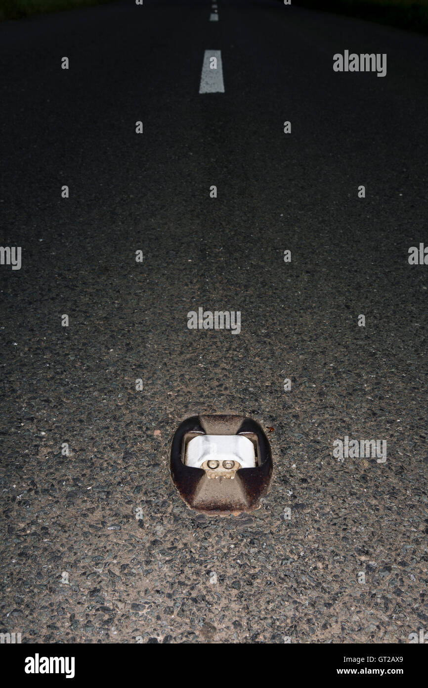 Cats eye in an asphalt road the tarmac black in the night lit by camera ...