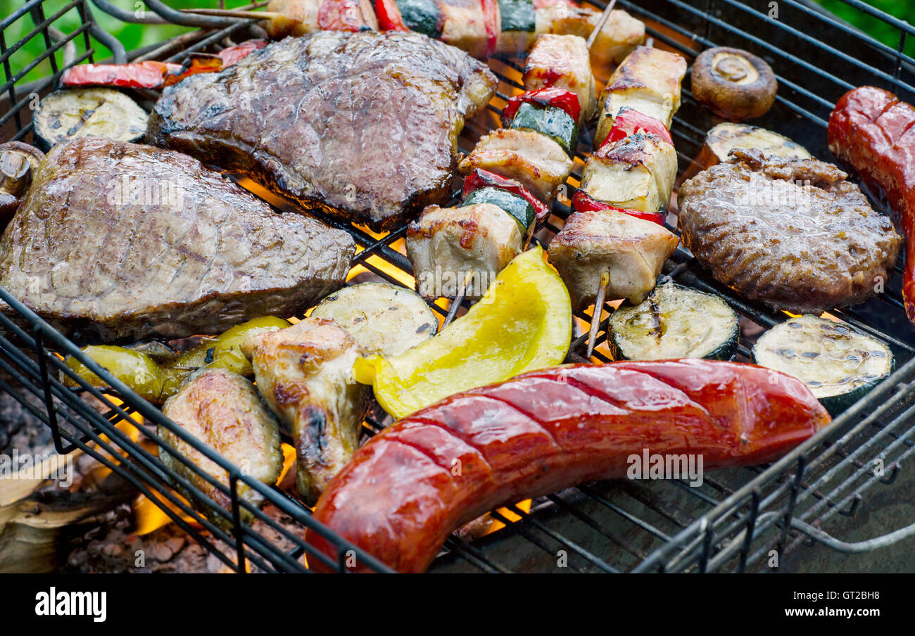 Assorted delicious meat with vegetables cooking on grill with flames ...