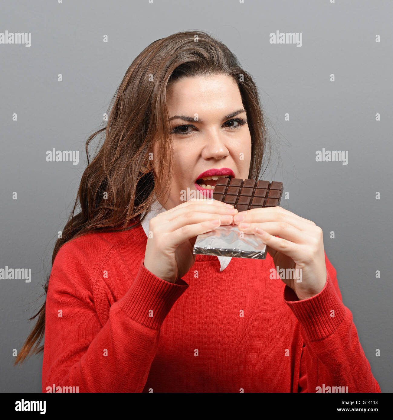 Beautiful woman eating chocolate against gray background Stock Photo ...